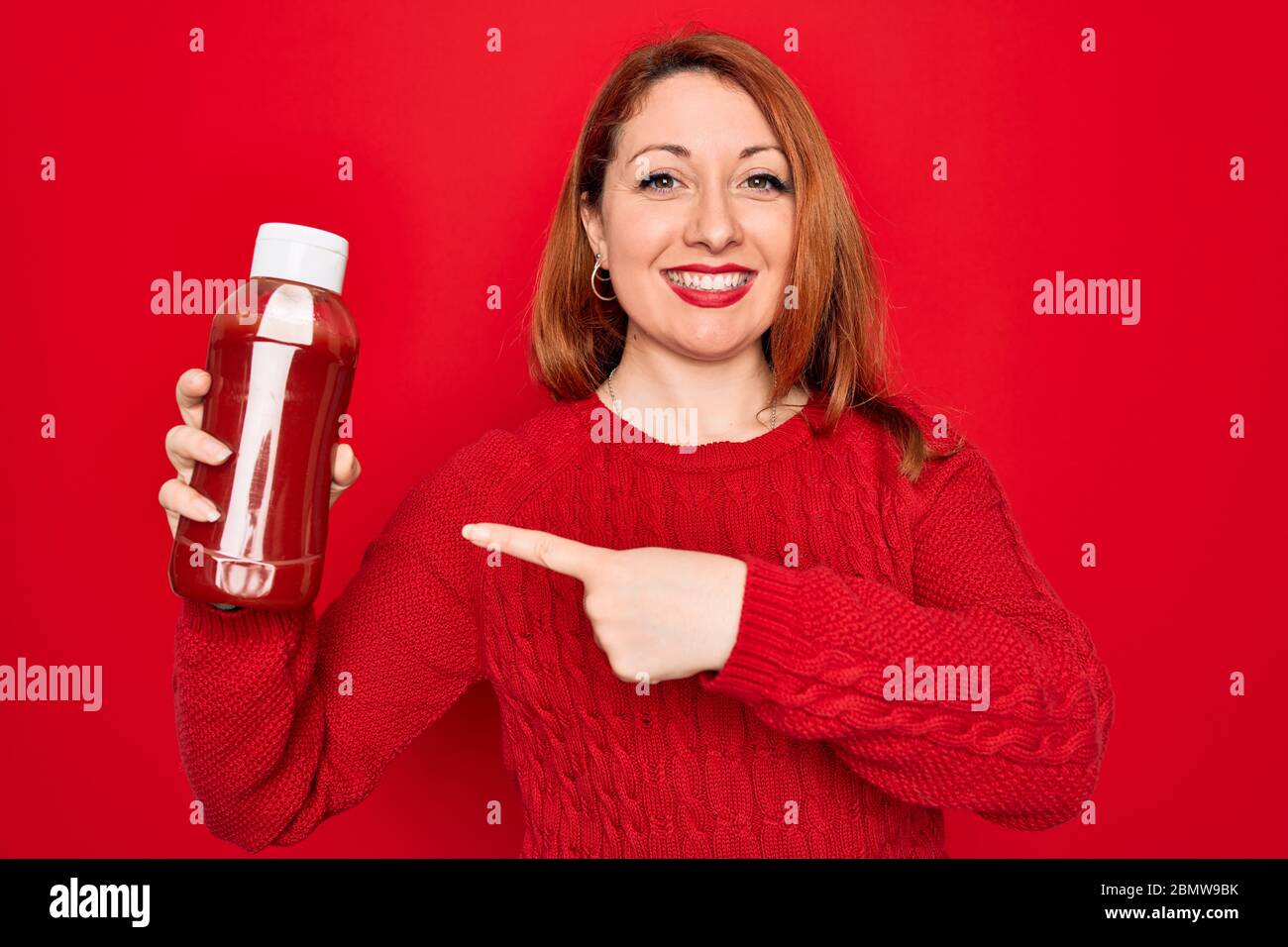 Beautiful redhead woman holding bottle of ketchup sauce condiment over ...