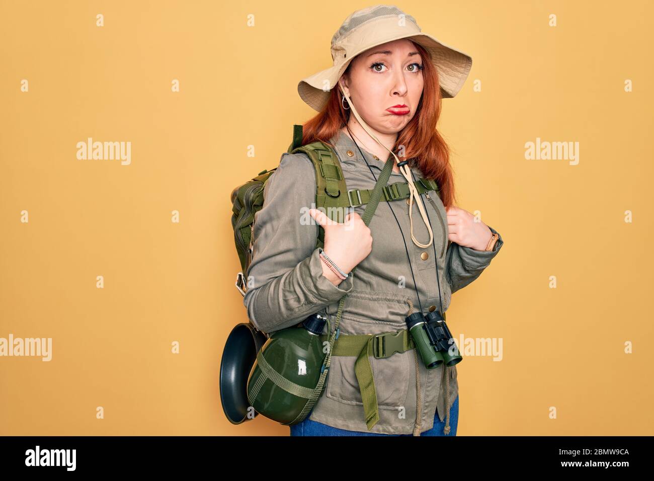 Young redhead backpacker woman hiking wearing backpack and hat over ...