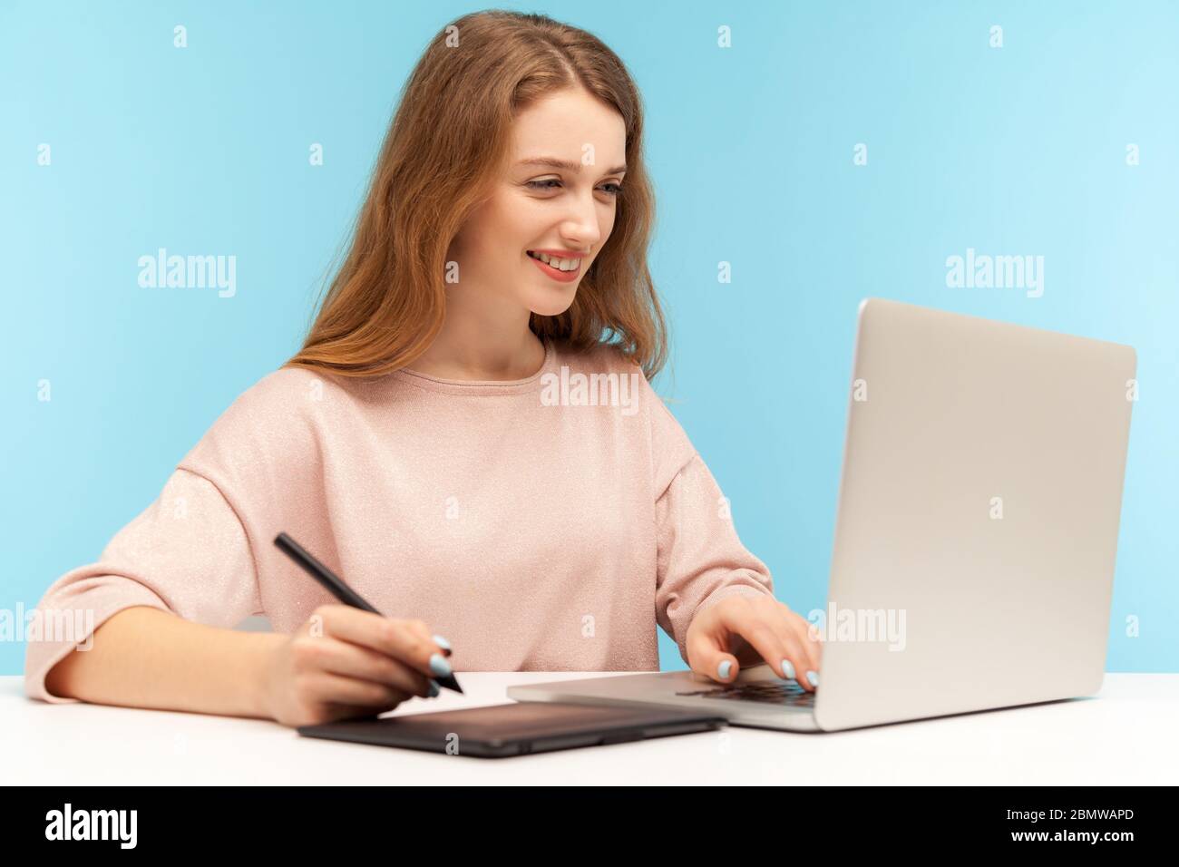 Charming smiling woman, creative designer using graphic tablet and typing keyboard laptop ...