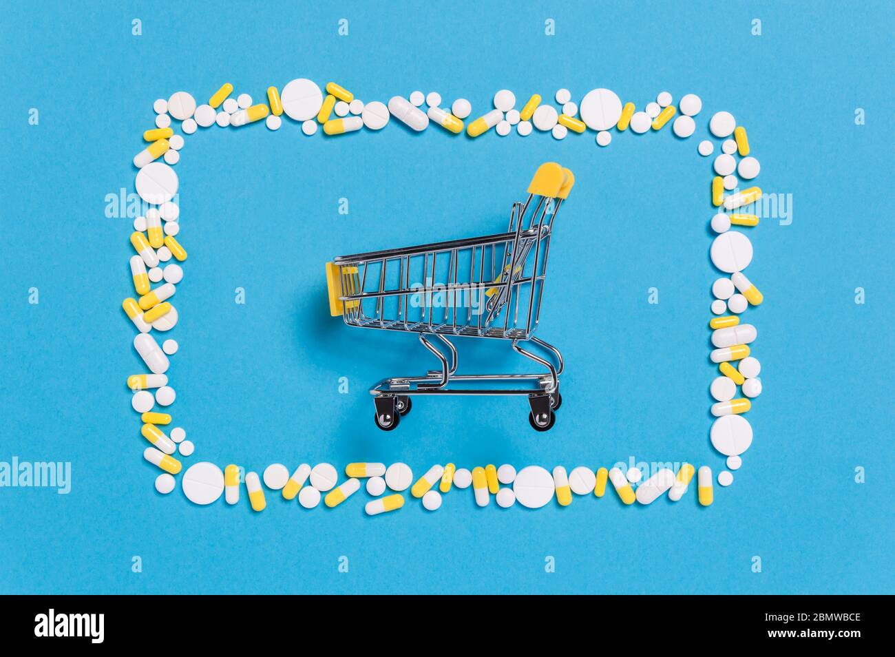 Yellow shopping cart in frame of white pills and capsules on blue ...