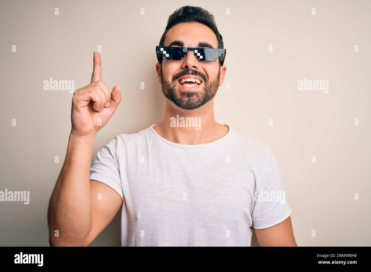 Young handsome man with beard wearing funny thug life sunglasses over ...