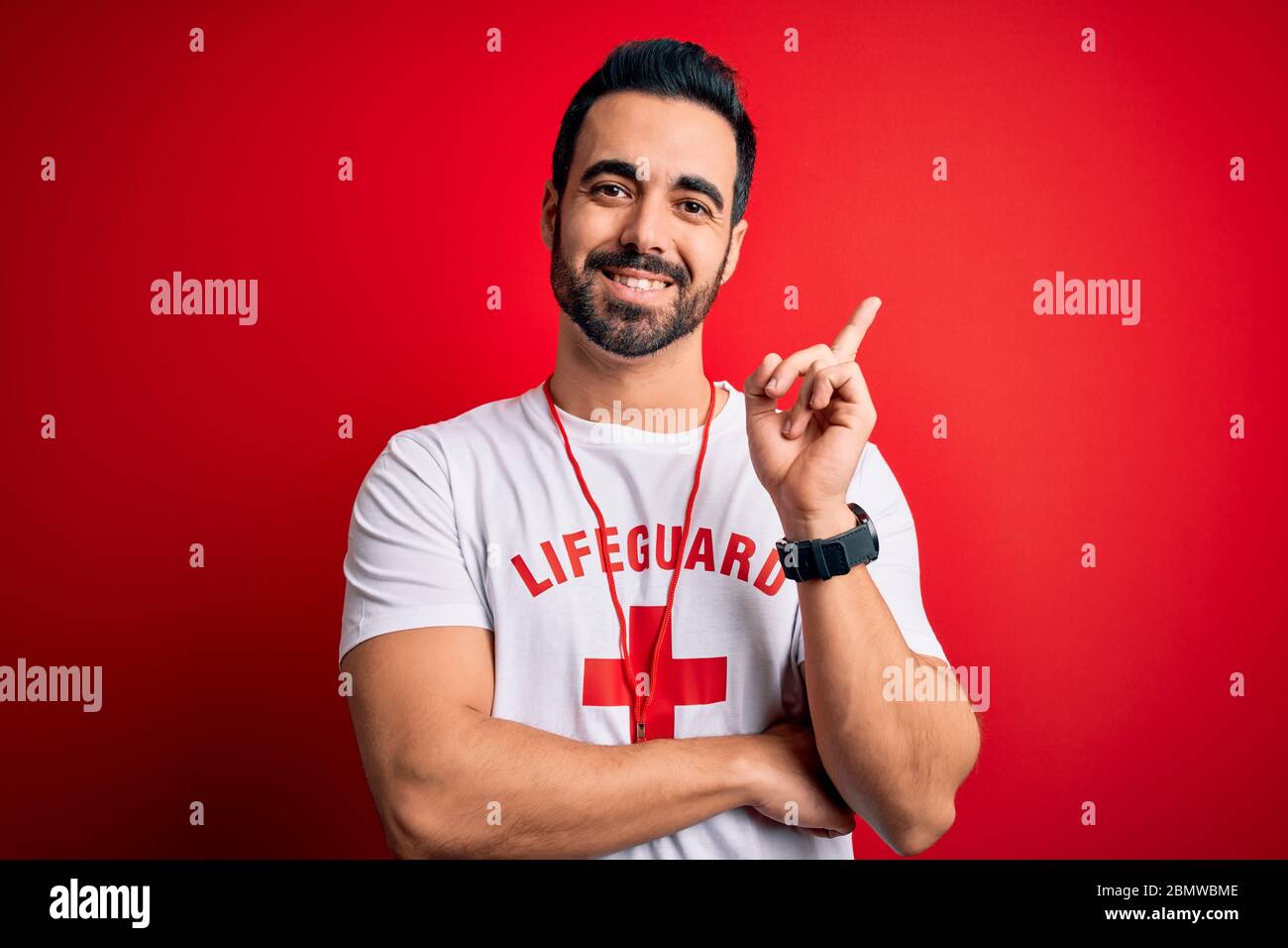 Young handsome lifeguard man with beard wearing whistle over isolated ...