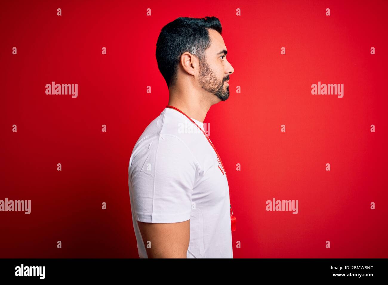 Young handsome lifeguard man with beard wearing whistle over isolated ...
