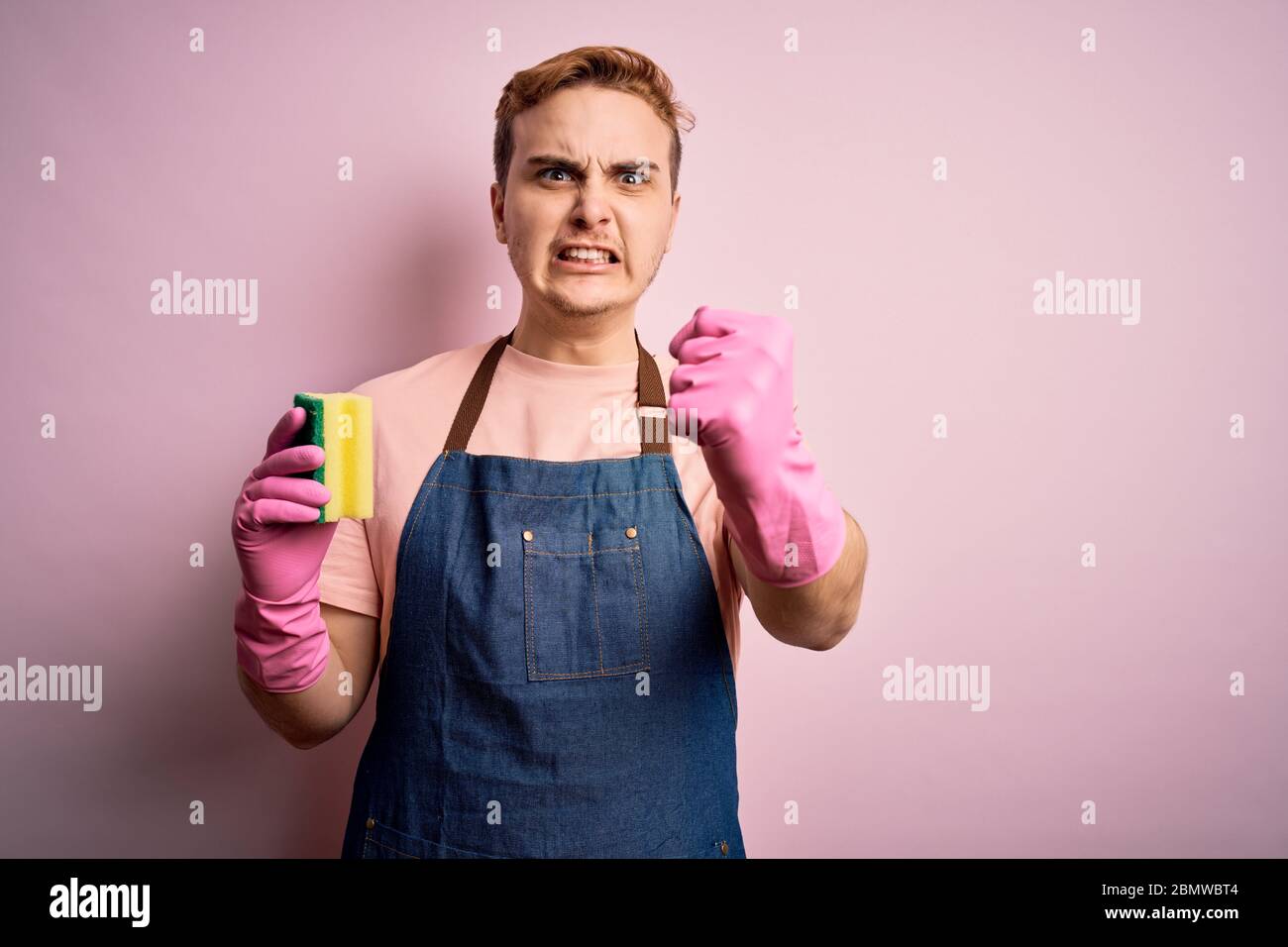 Handsome redhead man doing housework wearing apron and gloves using ...