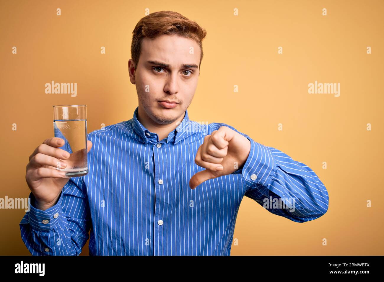 Young handsome redhead man drinking glass of water over isolated yellow ...