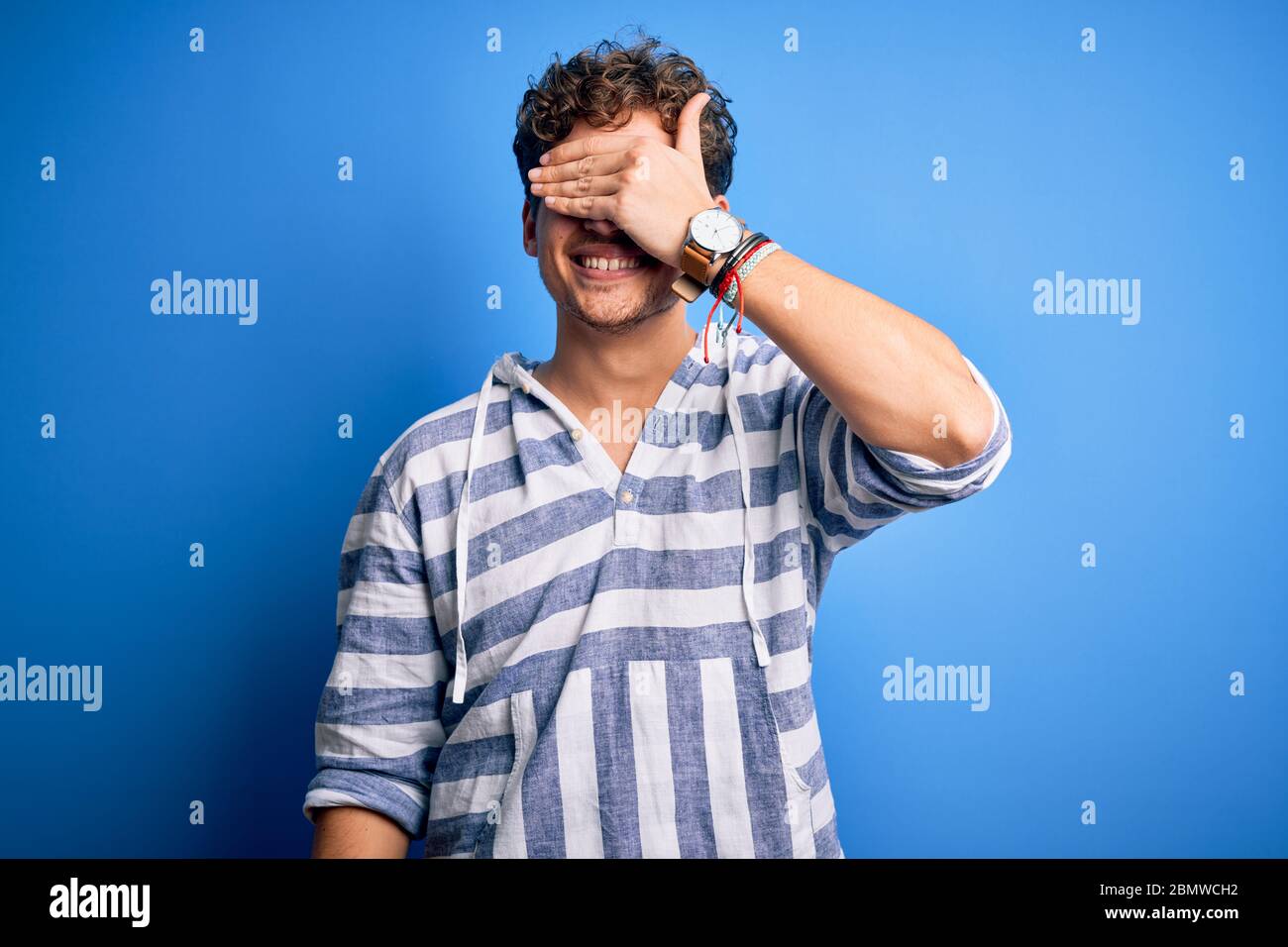 Young blond handsome man with curly hair wearing casual striped sweatshirt smiling and laughing ...