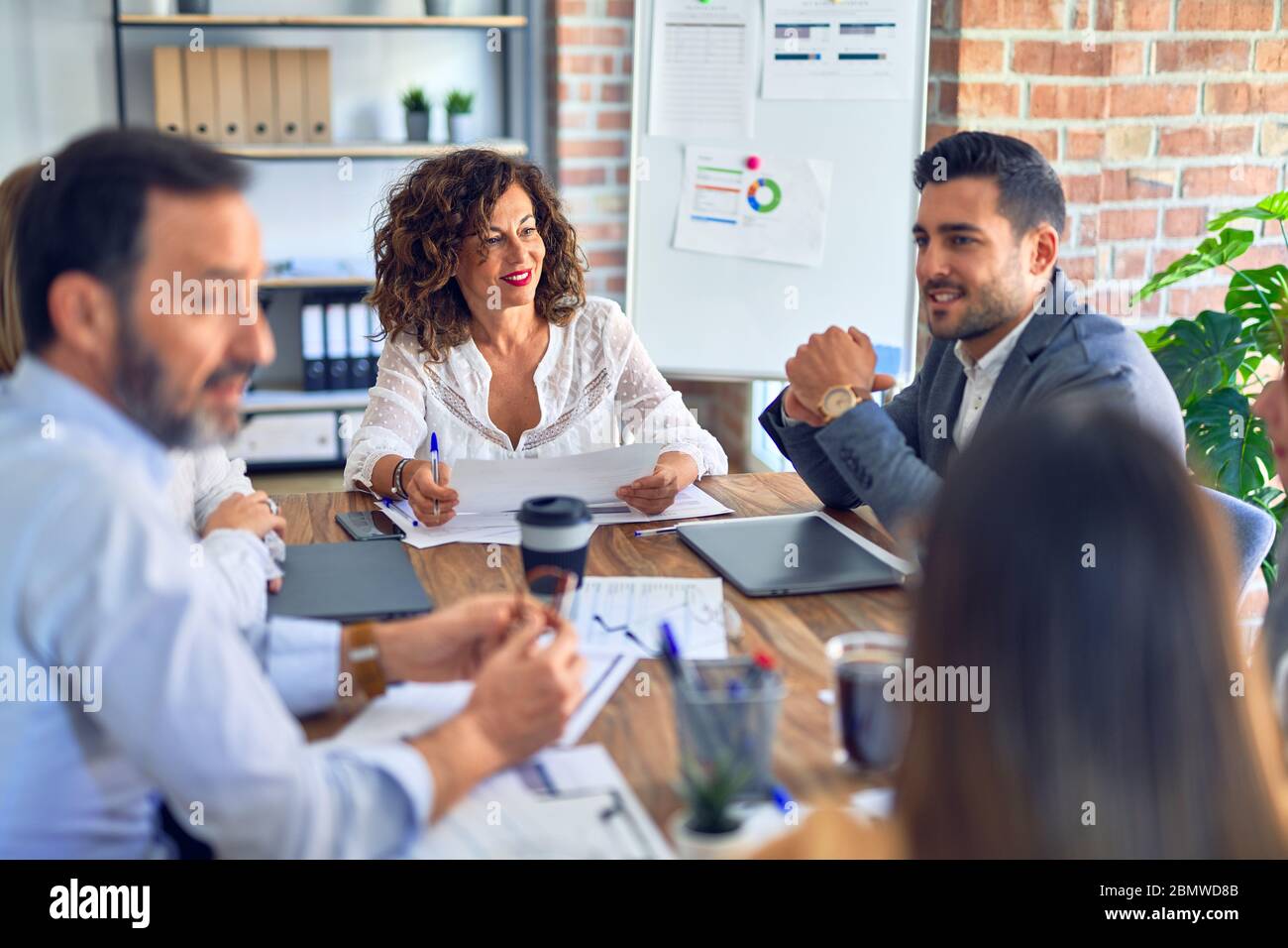 Group of business workers working together. Sitting on desk speaking at ...