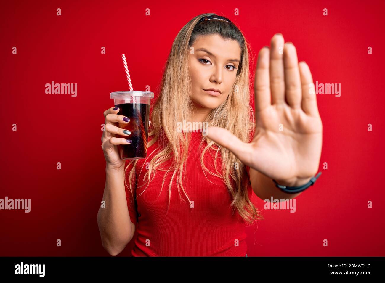 Young beautiful blonde woman drinking cola fizzy beverage using straw ...