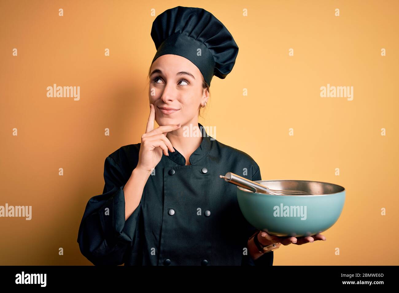 Young beautiful chef woman wearing cooker uniform and hat holding bowl ...