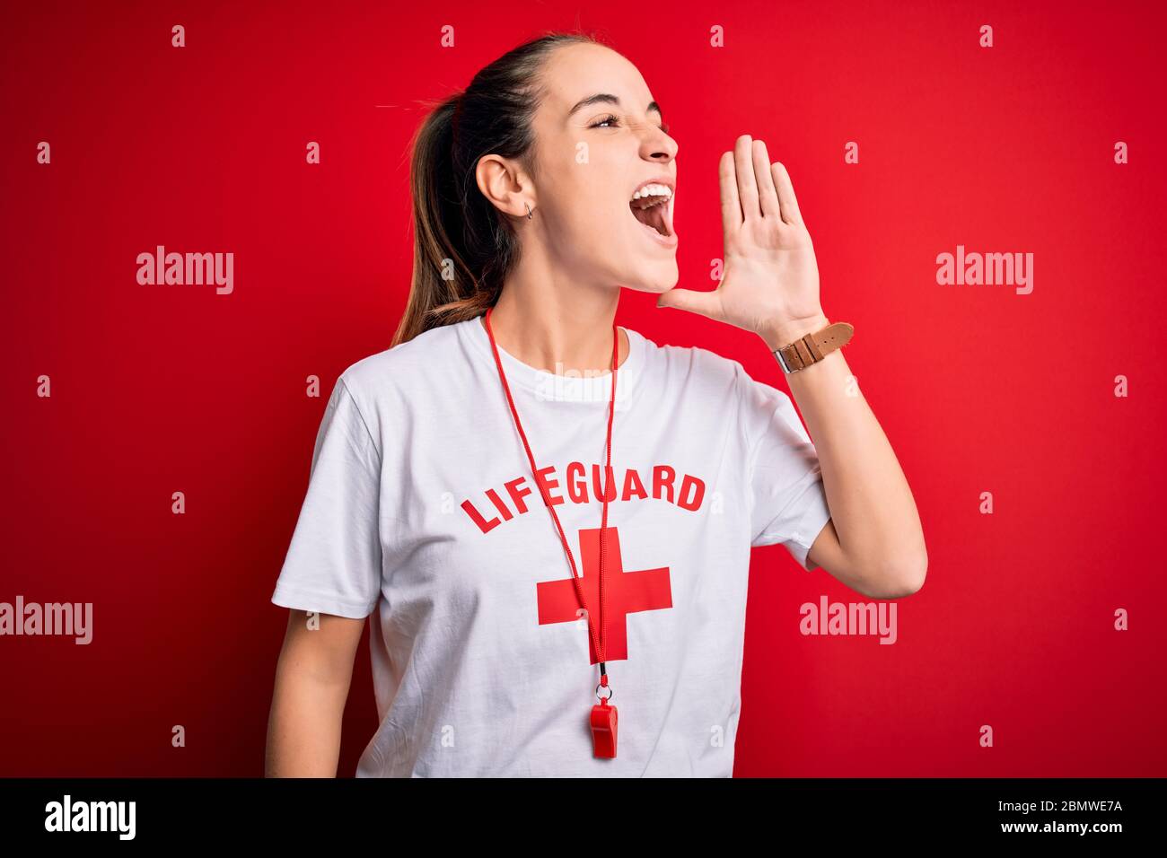 Beautiful lifeguard woman wearing t-shirt with red cross using whistle ...