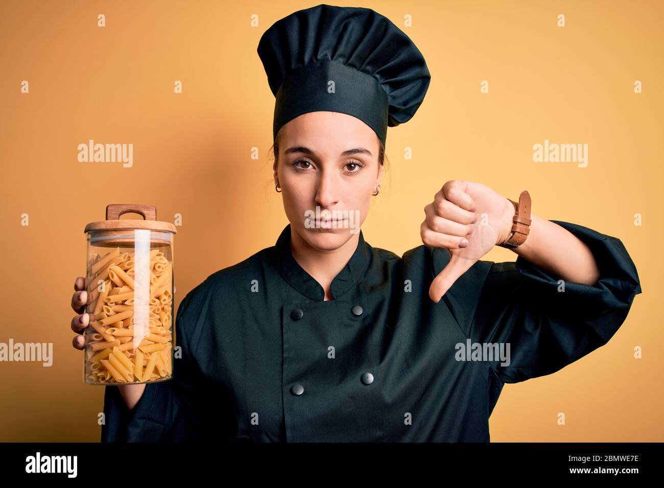 Young beautiful chef woman wearing cooker uniform holding jar with ...