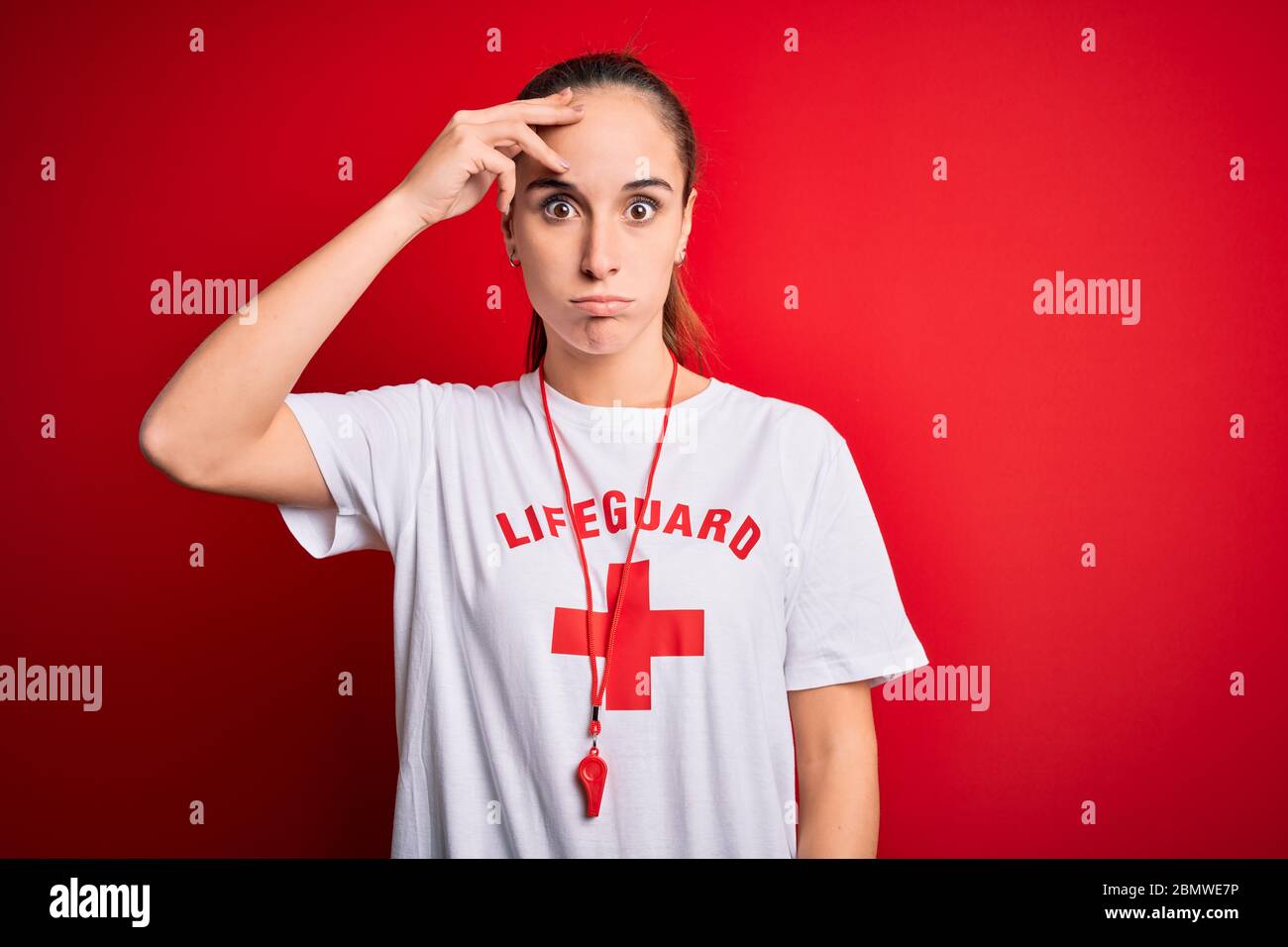 Beautiful lifeguard woman wearing t-shirt with red cross using whistle ...