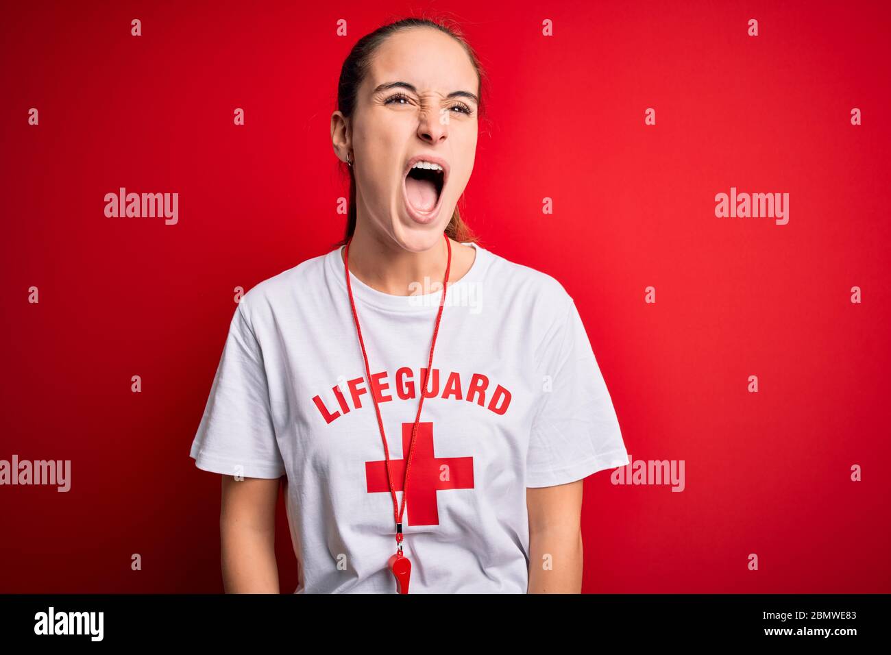 Beautiful lifeguard woman wearing t-shirt with red cross using whistle ...