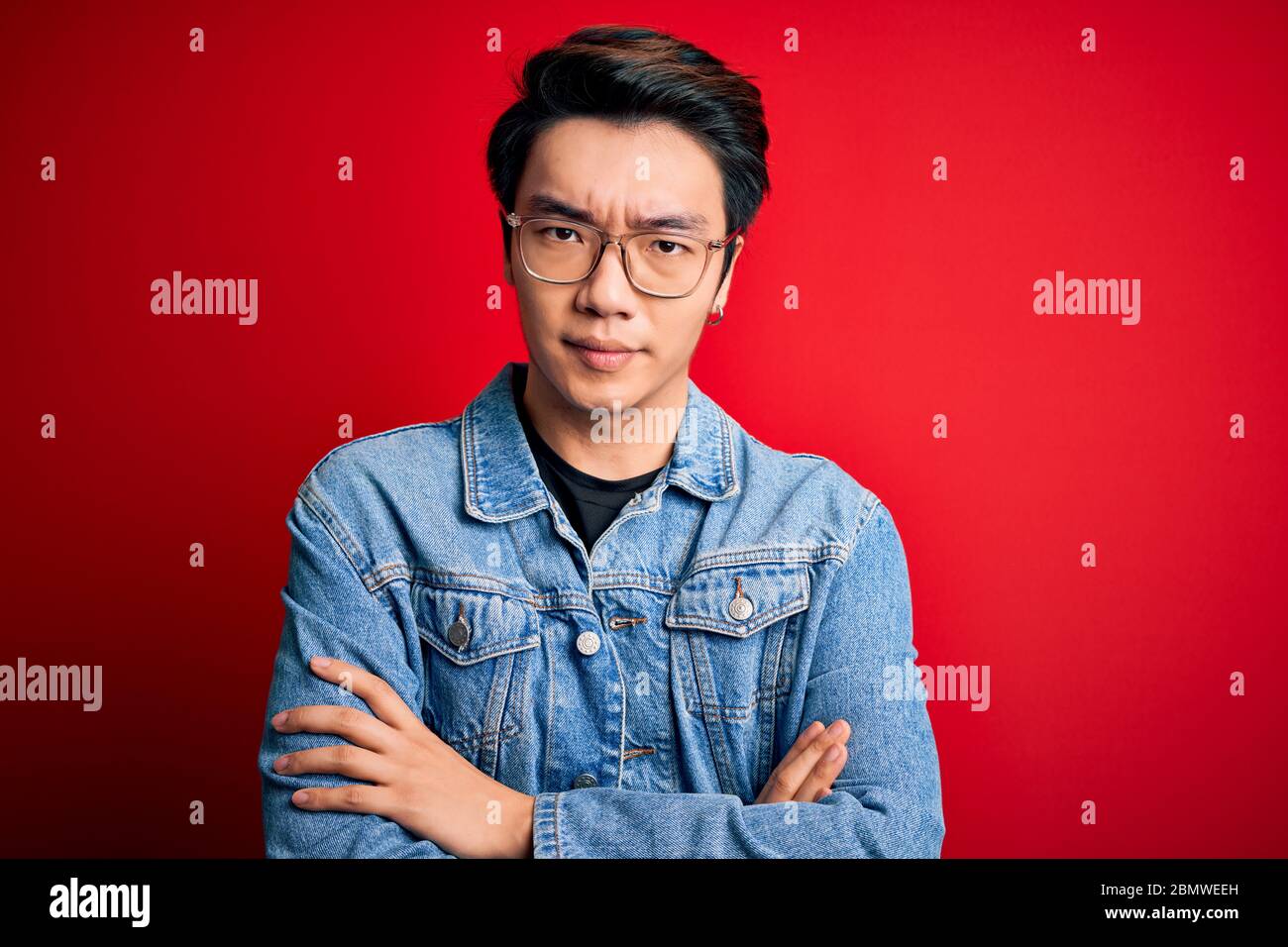 Young handsome chinese man wearing denim jacket and glasses over red ...