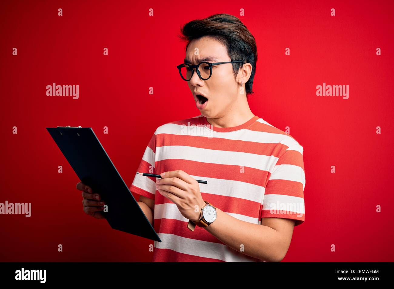 Young handsome chinese inspector man wearing glasses holding clipboard ...