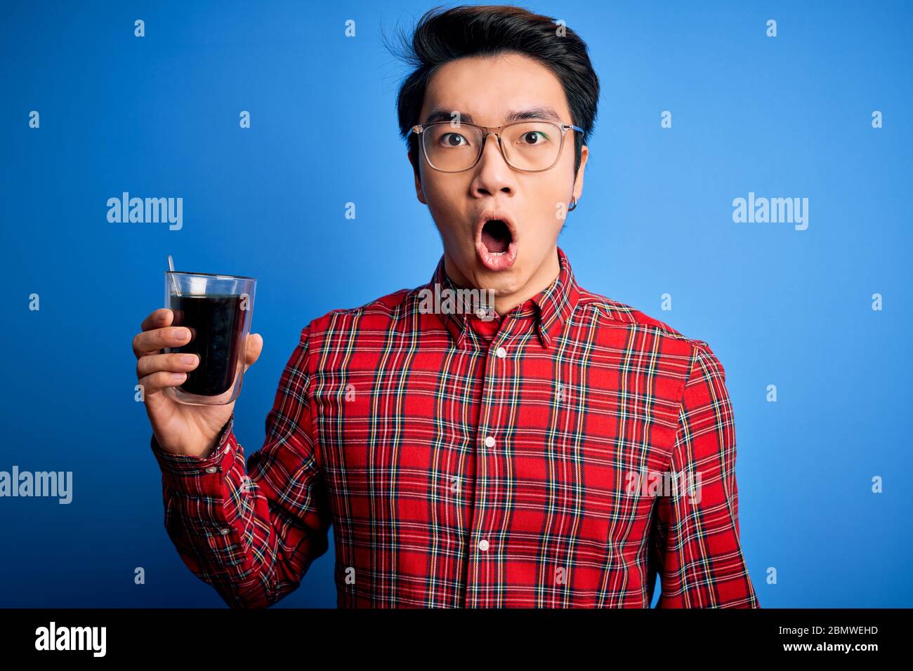 Young handsome chinese man drinking glass of coffee over isolated blue ...