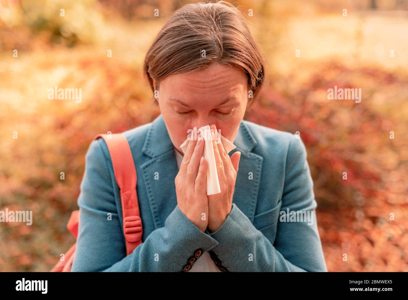 Businesswoman nose-blowing paper tissue in autumnal park during the ...