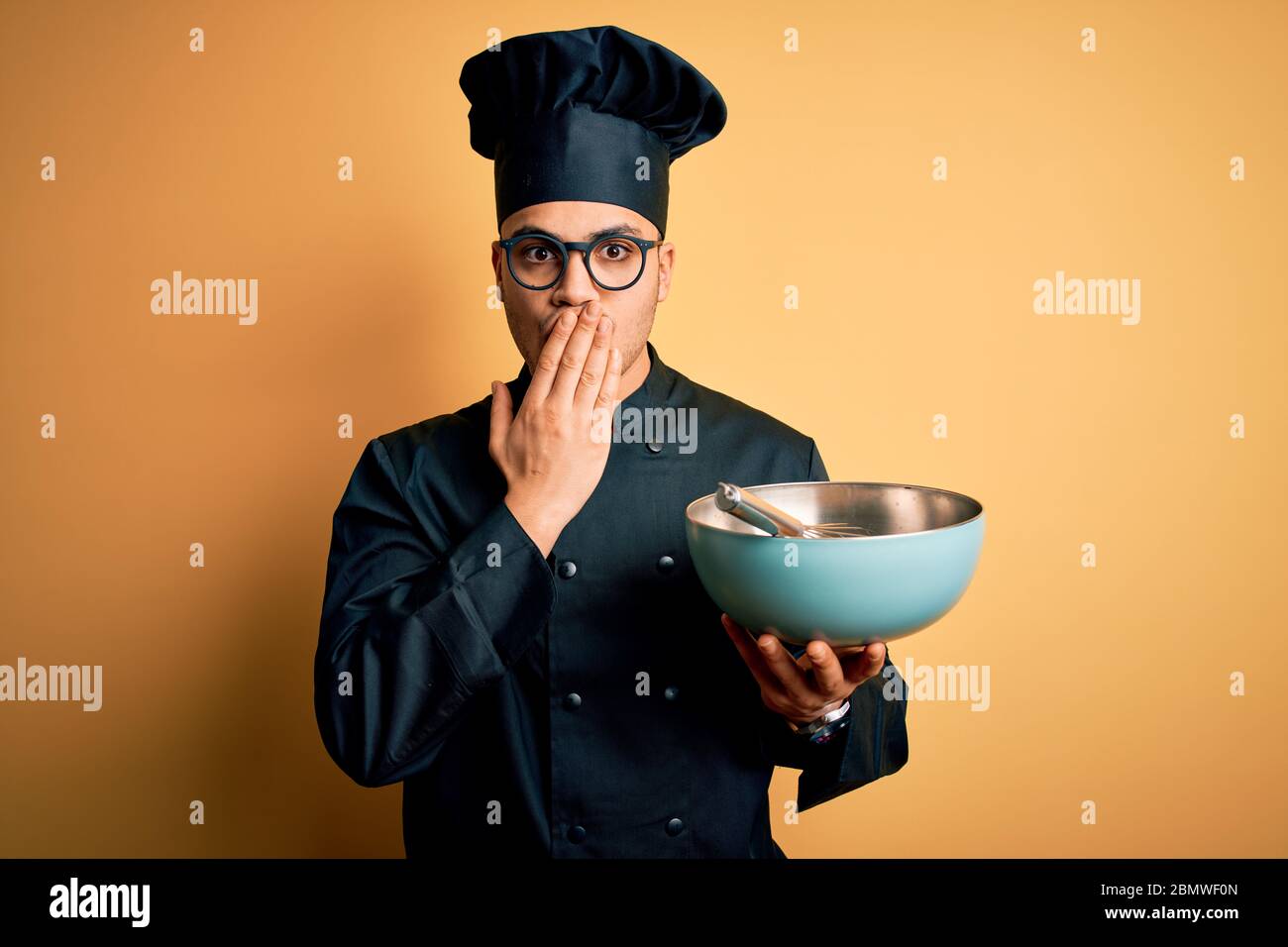 Young brazilian chef man wearing cooker uniform and hat using bowl and ...
