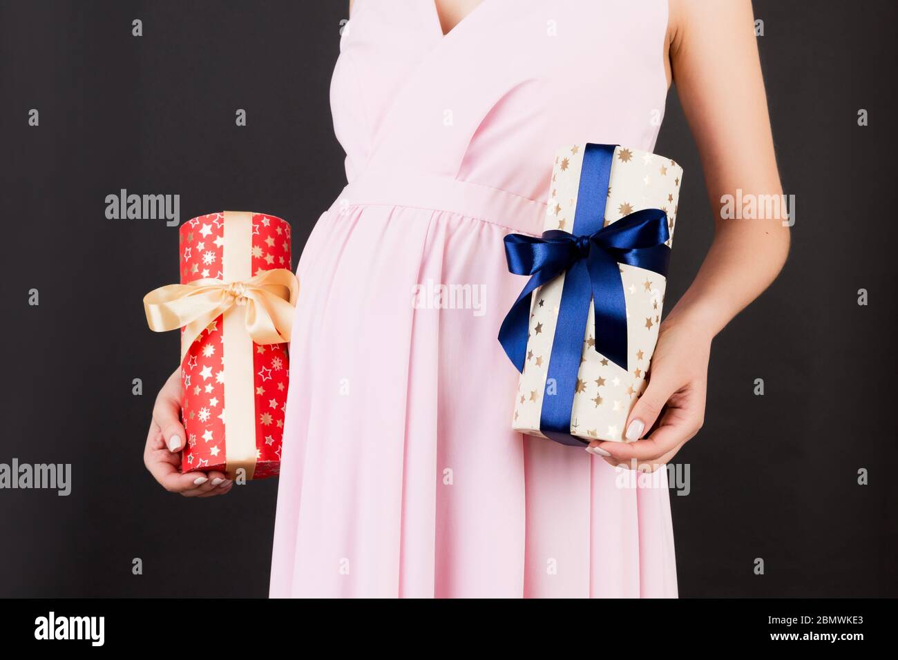 Close up of pregnant woman in pink dress holding two gift boxes at ...