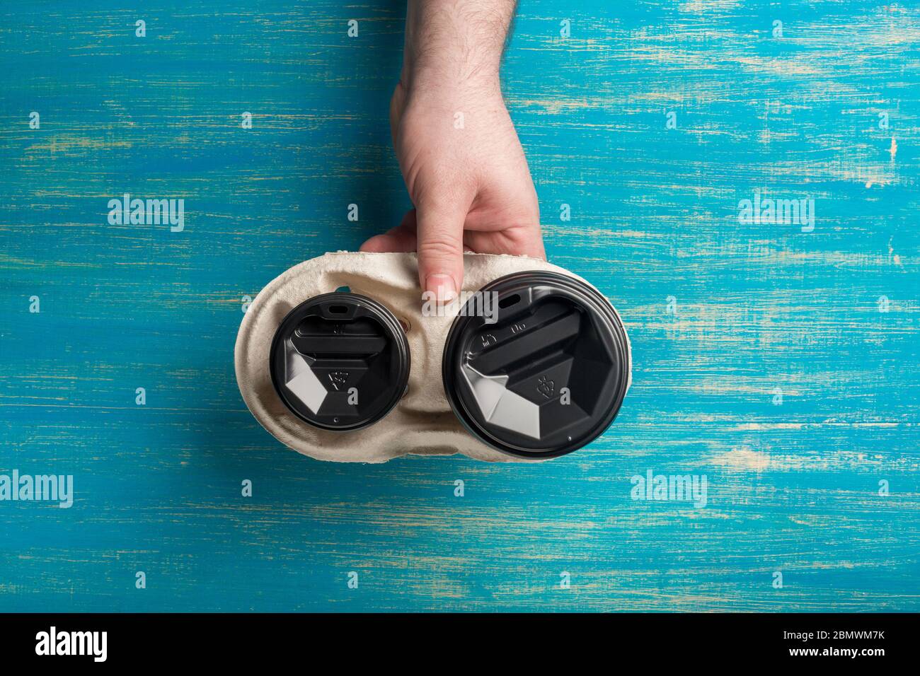 Two disposable paper cups of coffee and a cup holder in a male hand on ...