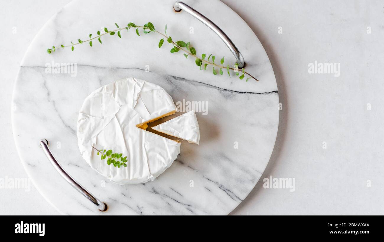 Round Brie cheese with a section cut out on a marble tray on white ...