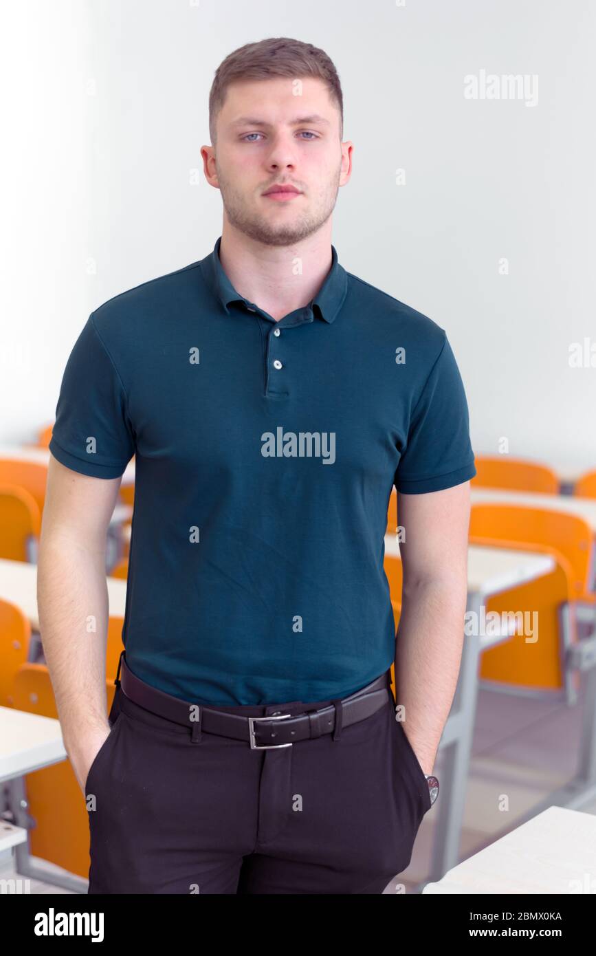 Smiling male student standing in classroom and looking at camera ...
