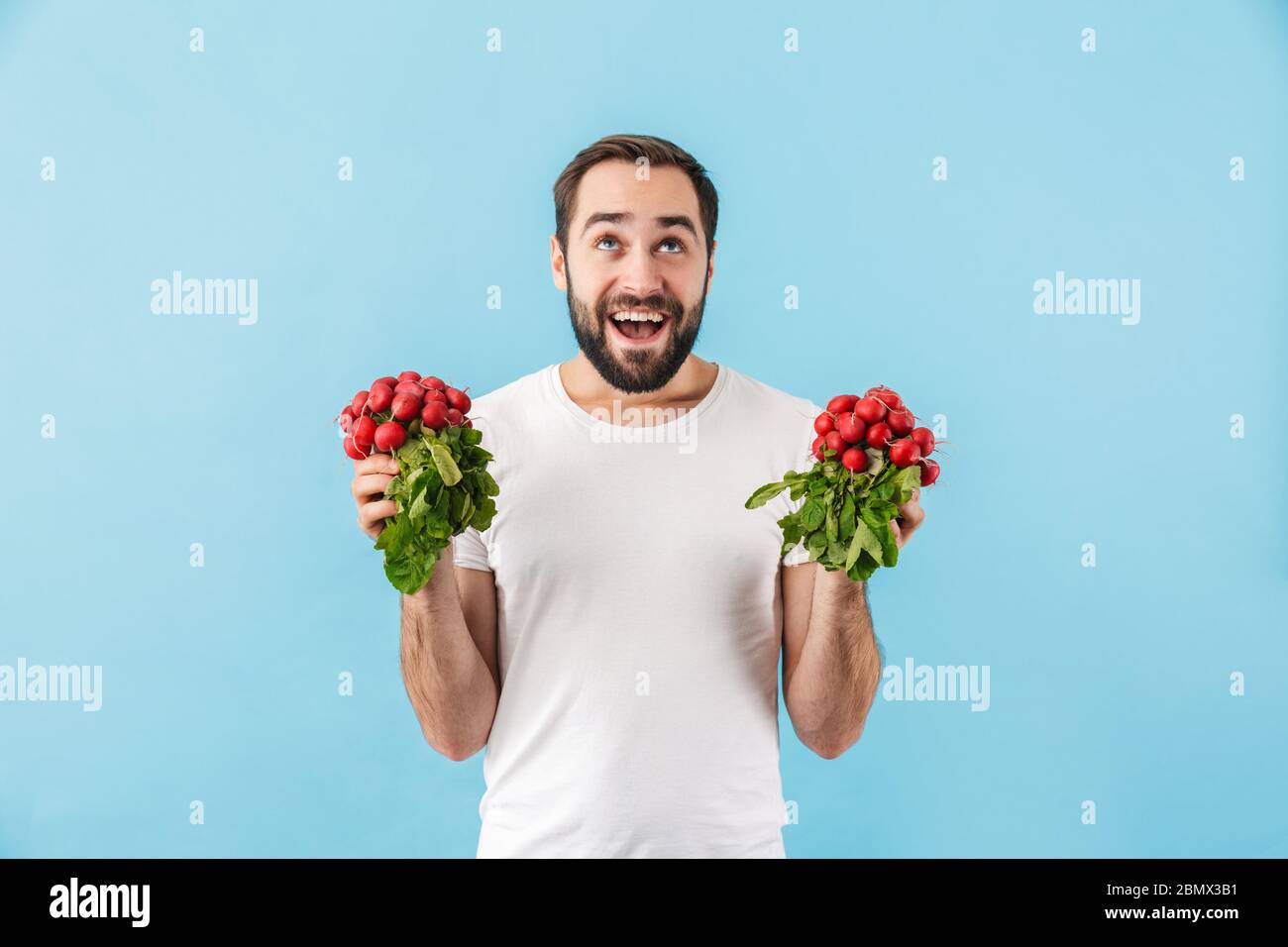 Portrait of a young cheerful excited bearded man wearing t-shirt standing isolated over blue ...
