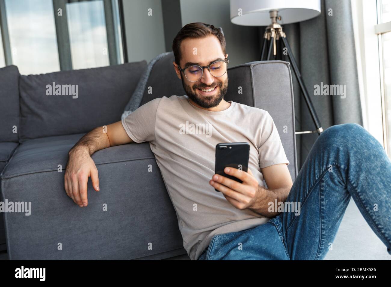 Attractive smart young man sitting on a floor in the living room, using ...