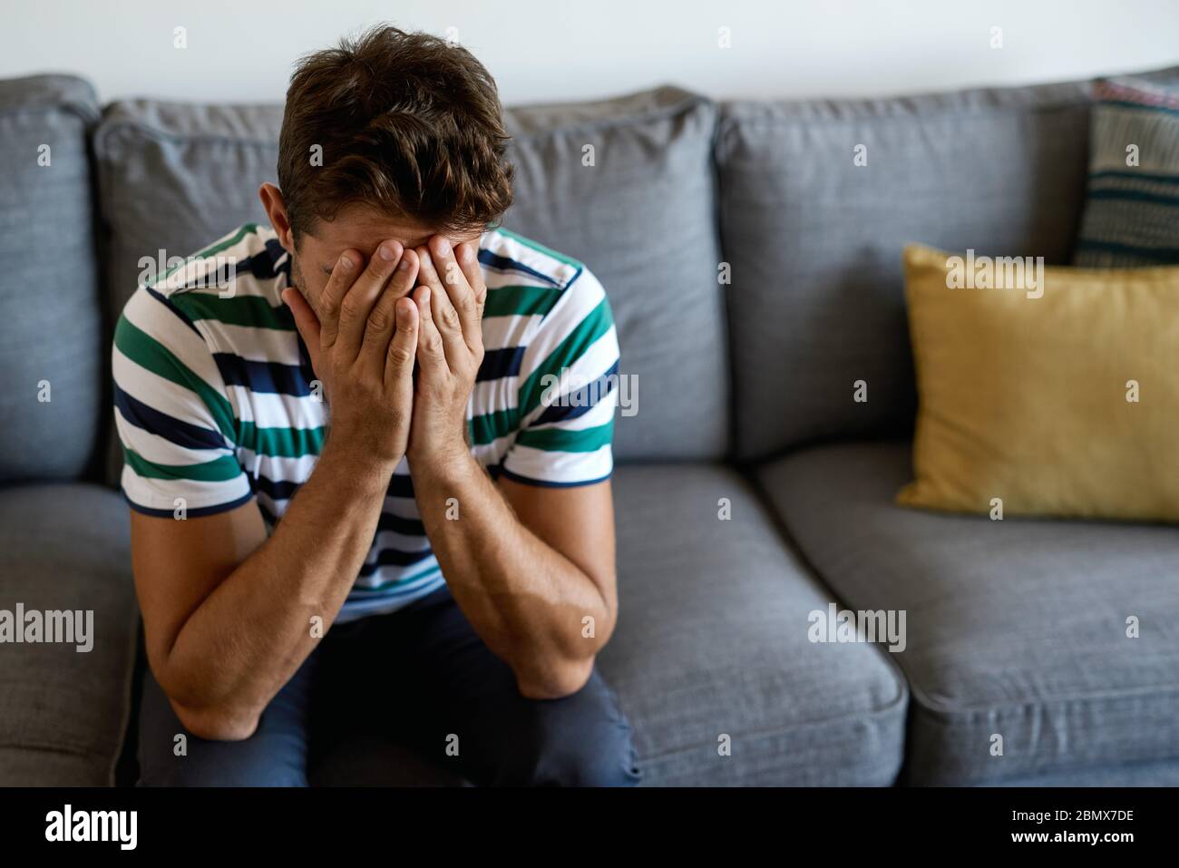 Young man sitting on his sofa looking distraught Stock Photo - Alamy