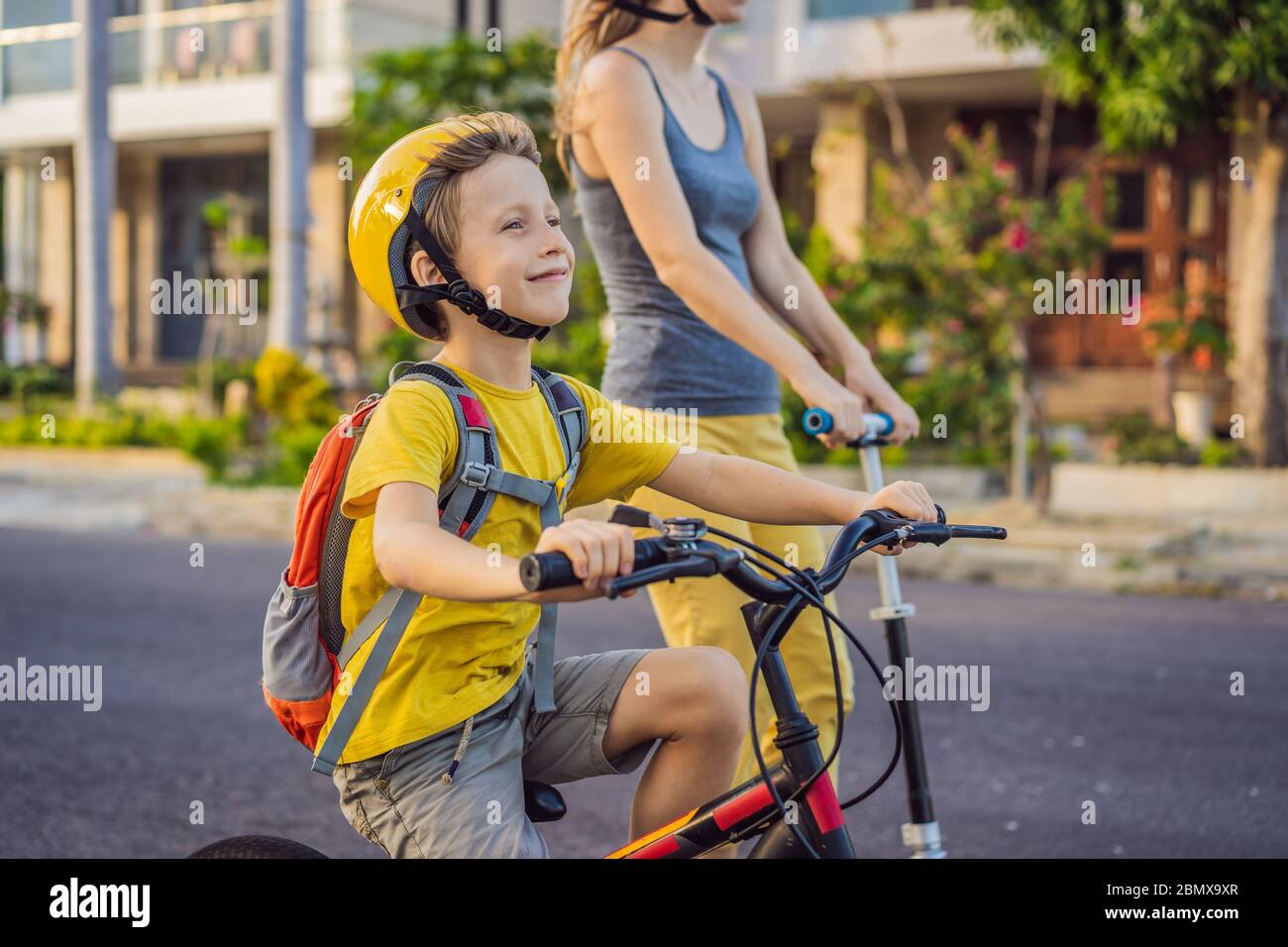 Active school kid boy and his mom in safety helmet riding a bike with ...