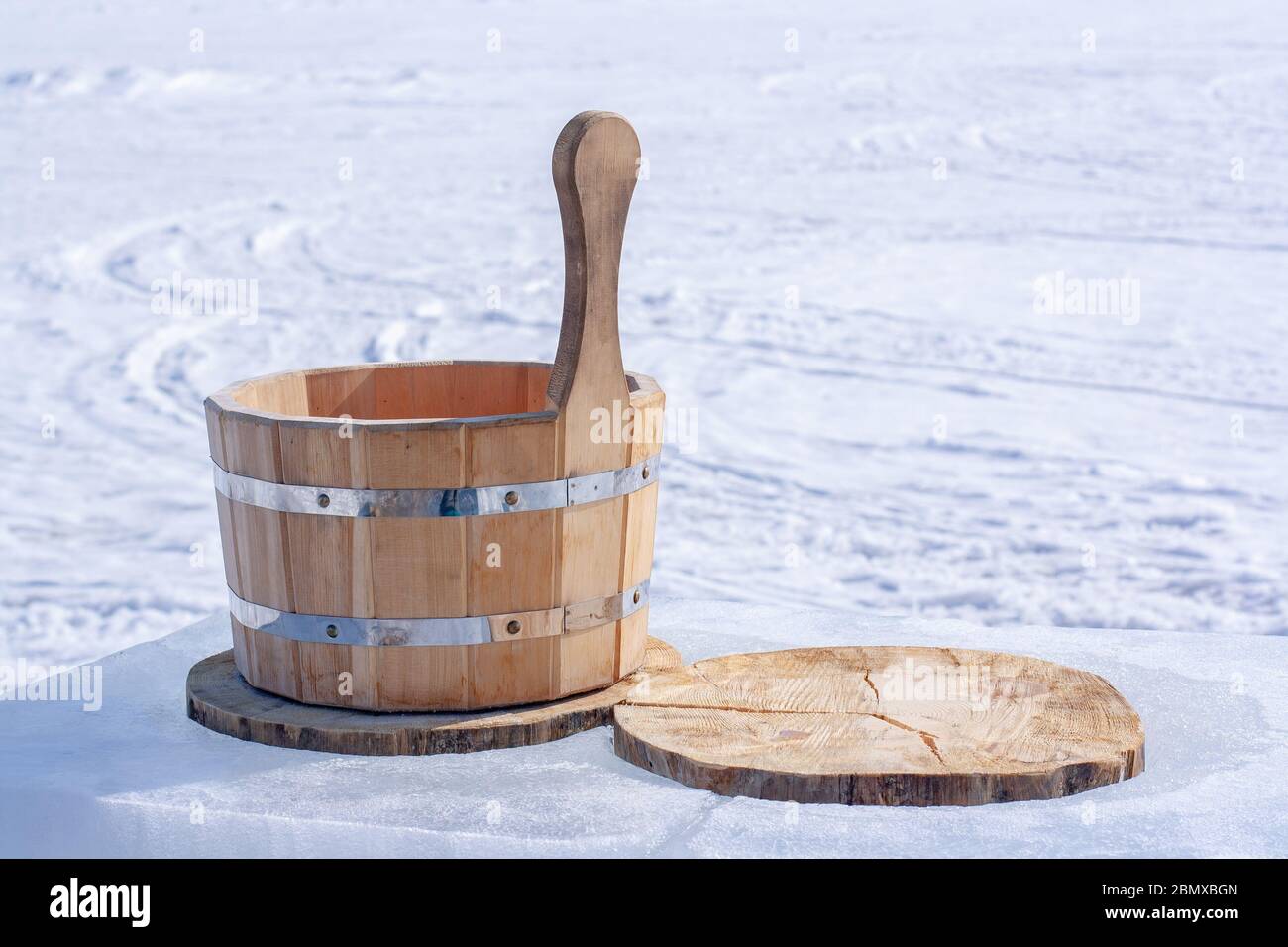 A wooden tub for water stands on a slice of a tree trunk on ice on a ...