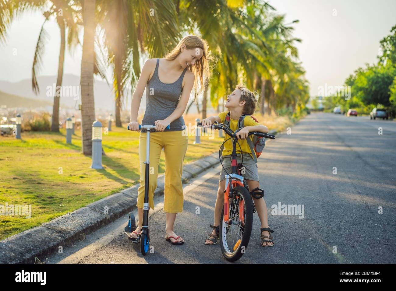 Active school kid boy and his mom riding a bike with backpack on sunny ...