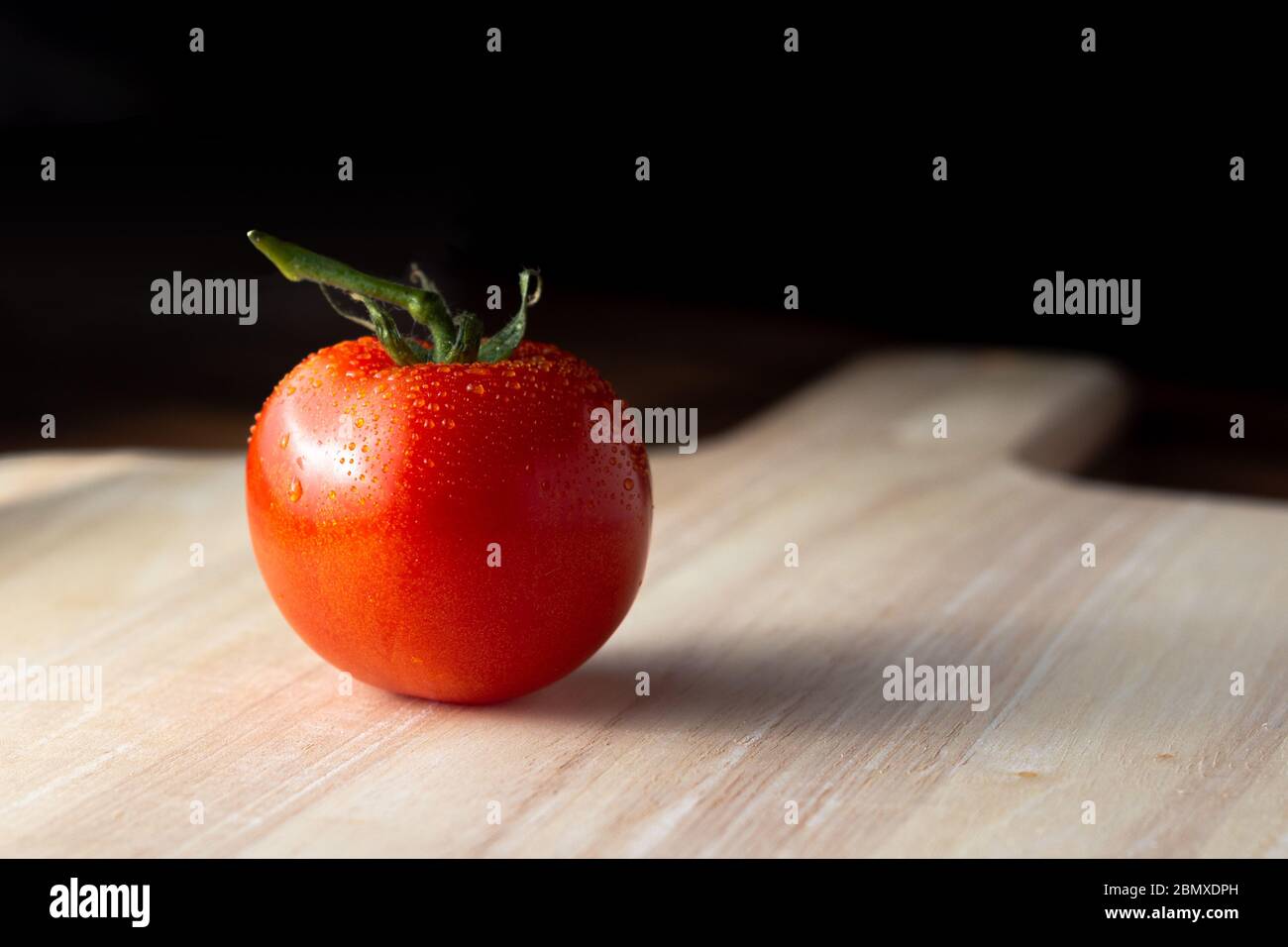 A single tomato viewed from the side sitting on a wooden board. The ...