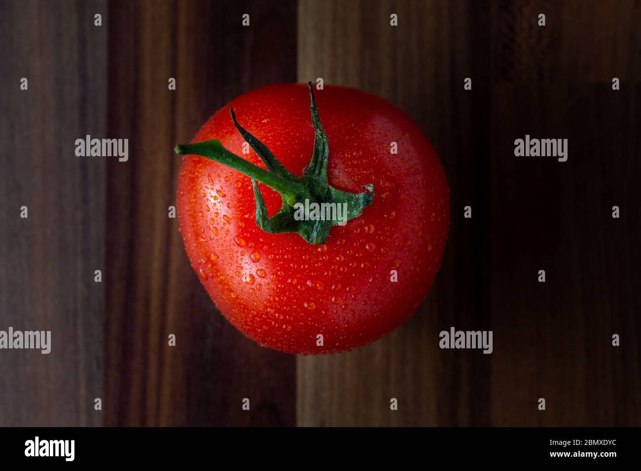 A single tomato viewed from the top down sitting on a wooden work ...