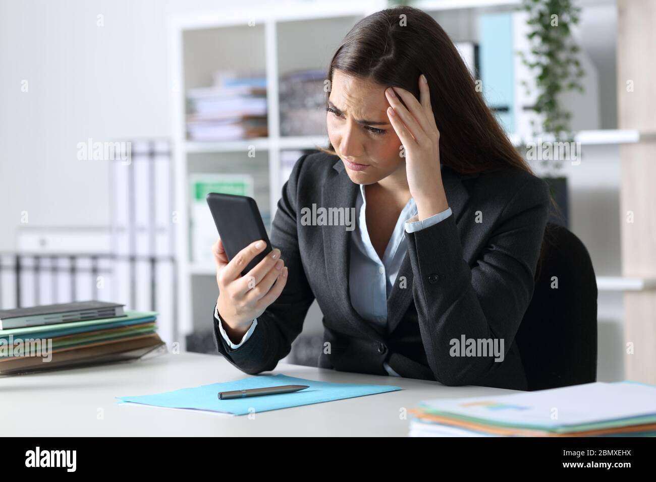 Sad executive woman reading bad news on smart phone sitting on a desk ...