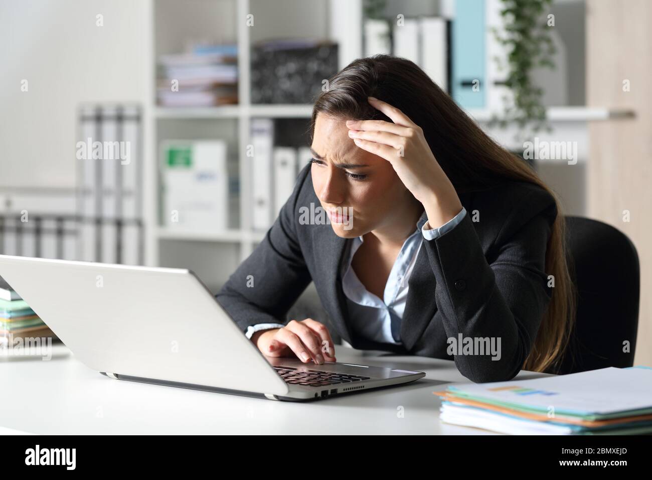 Sad executive woman reading bad news on laptop sitting on her desk in ...
