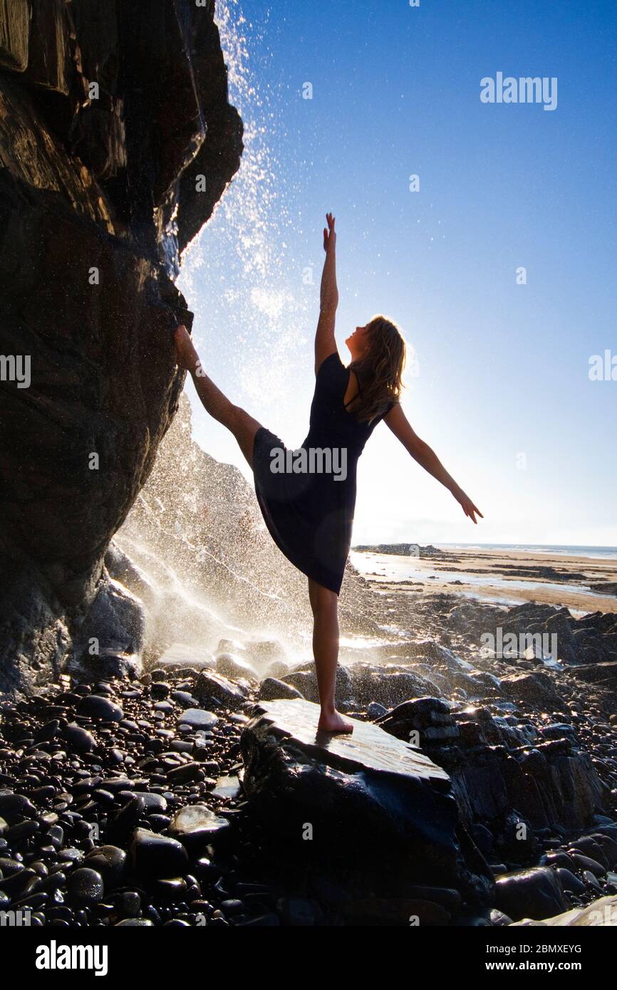 A young female dancer doing stretching exercises under a water fall ...