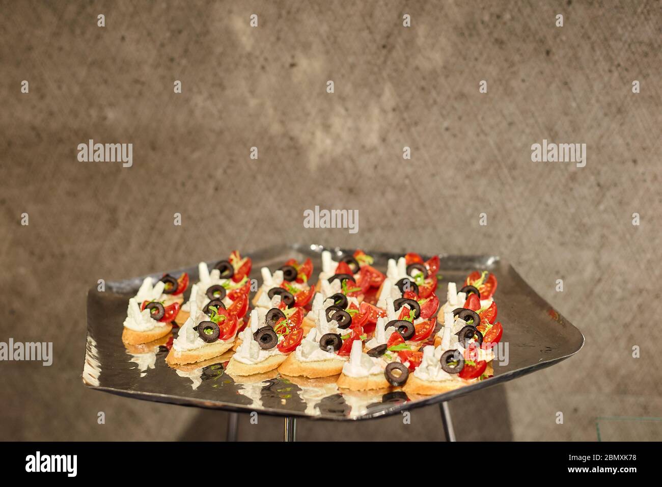 Canapes with olives, feta cheese, tomatoes and herbs lying in rows on a ...