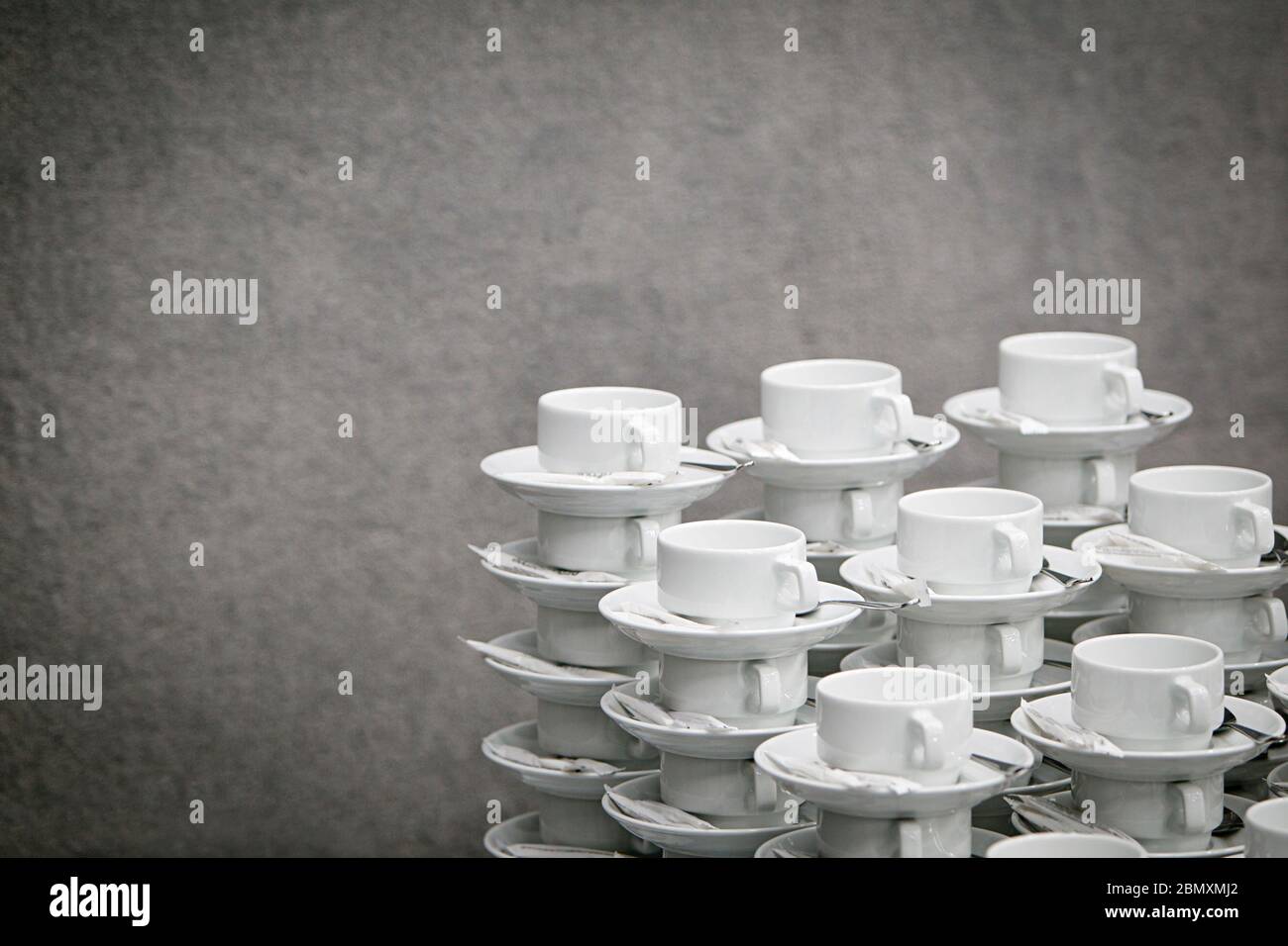 Piles of empty white ceramic cups with saucers, teaspoons and sachets ...