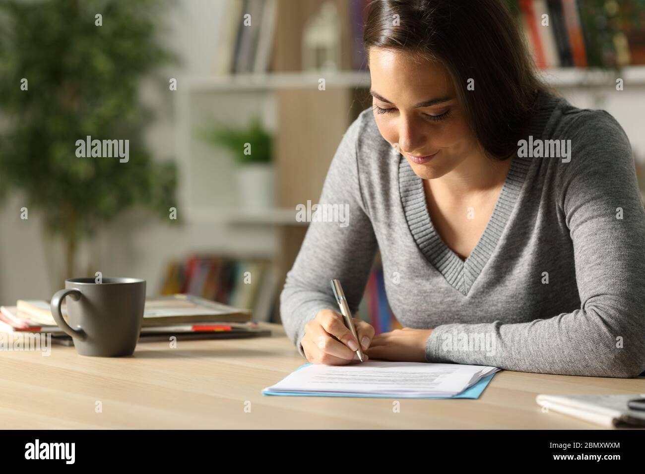 Girl signing document sitting on a desk in the living room at home in ...