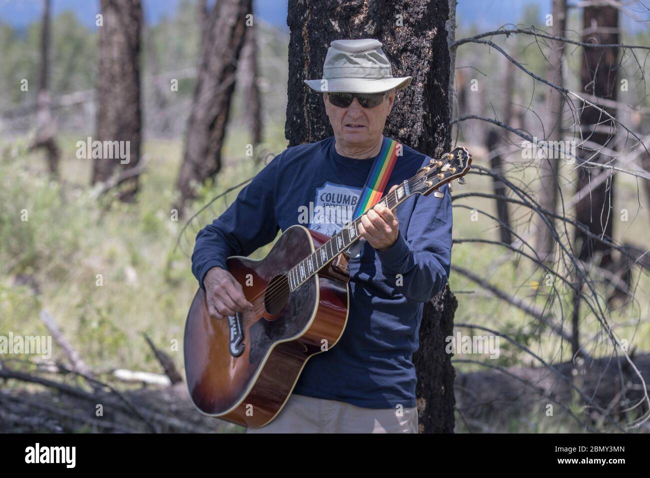 Man playing guitar, outdoors, standing in grass field, with blue sky ...