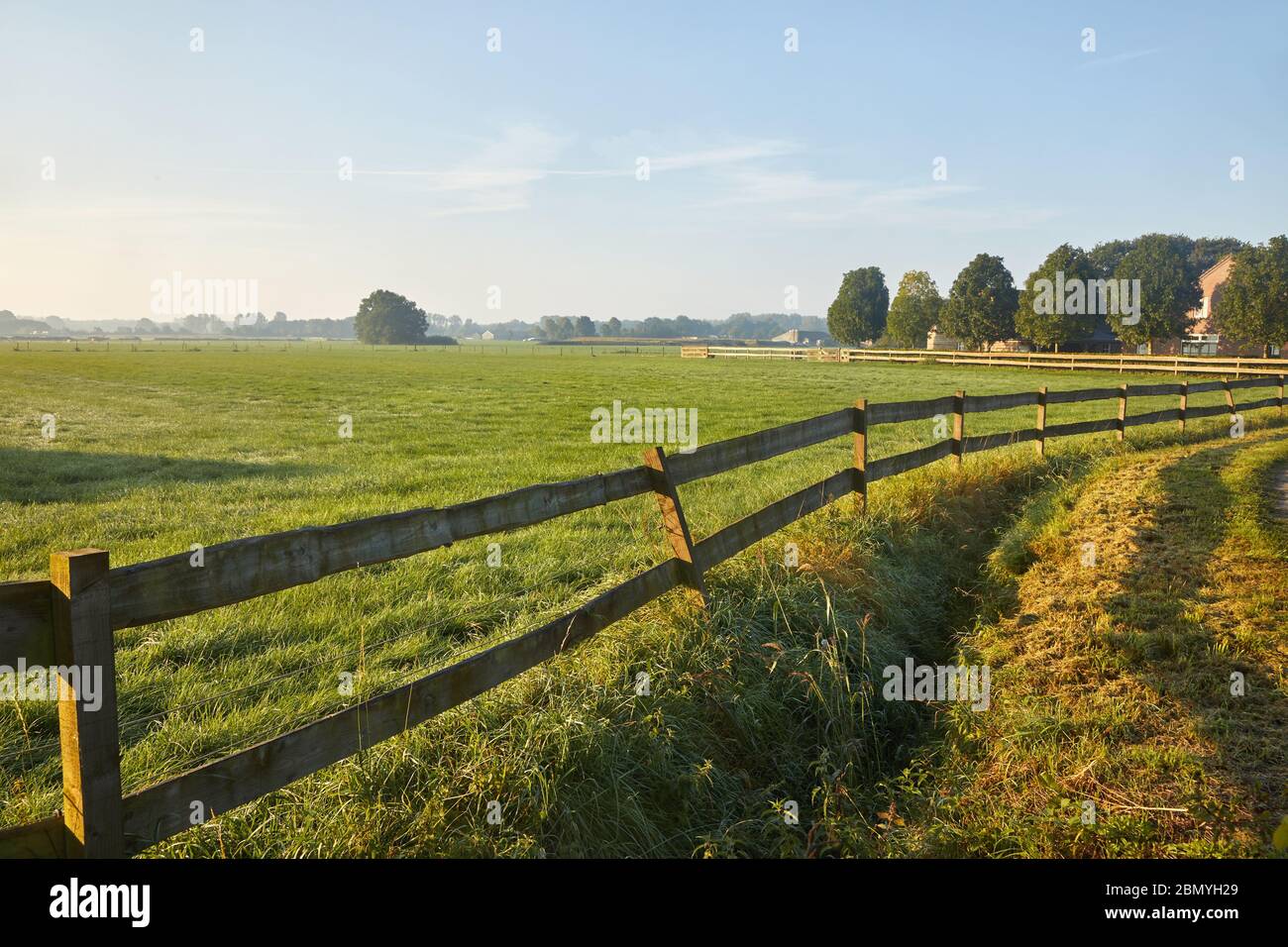 Green field with fence by a village Stock Photo - Alamy