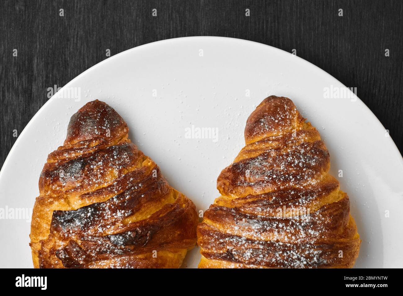 Flat lay of two buttery croissants on a white plate on a black ...