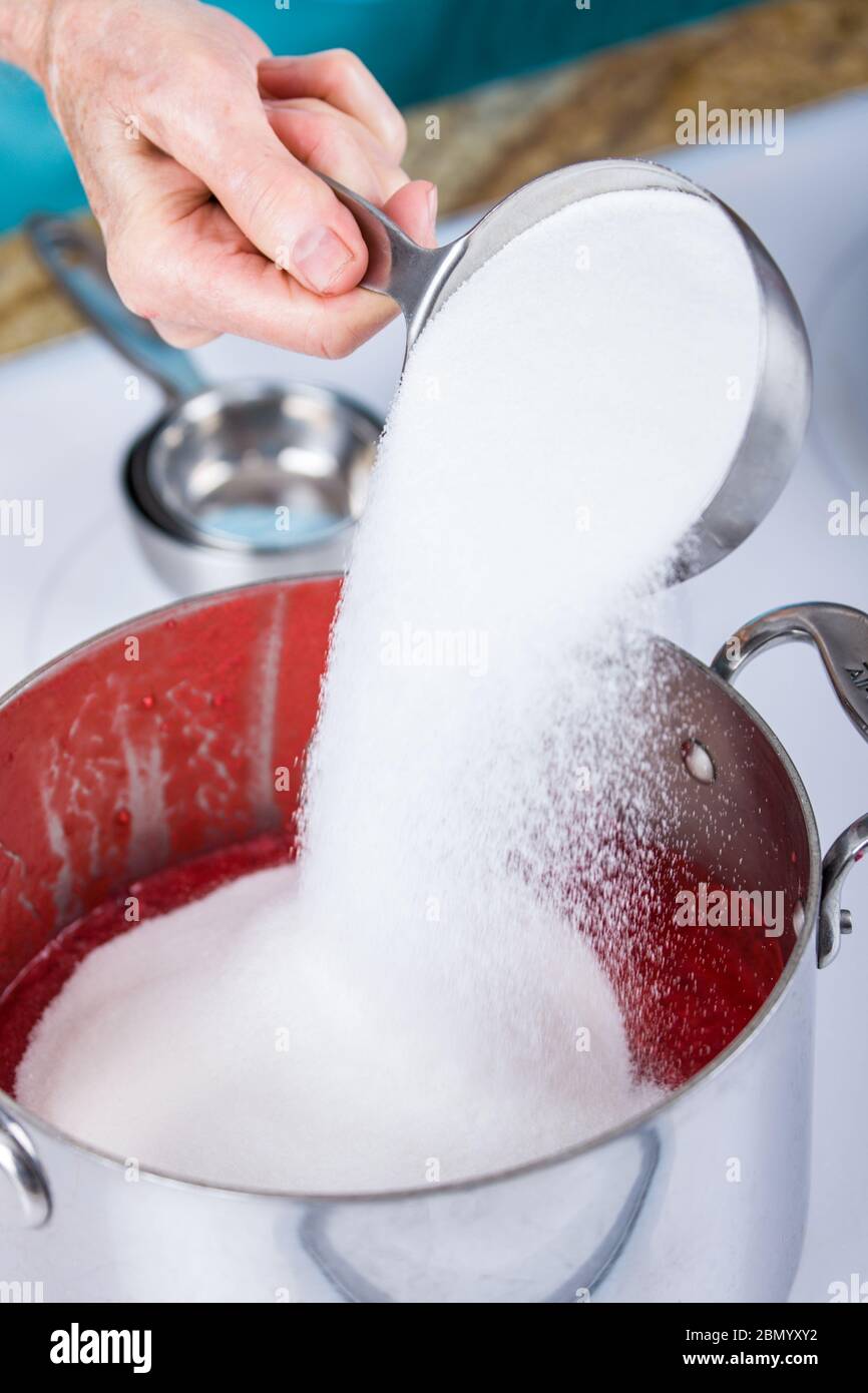 Woman pouring sugar into mashed berries for jam-making. When sugar is ...