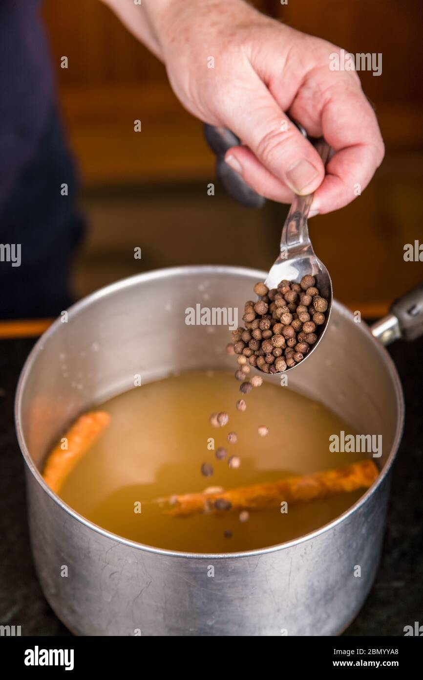 Woman pouring whole allspice into a pickling solution which will be ...
