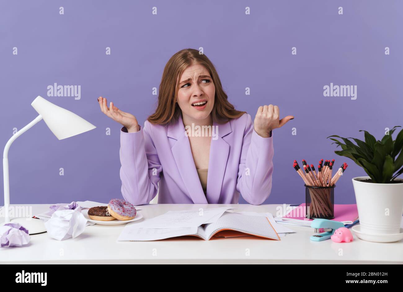Image of a confused woman sit at the table indoors isolated over purple ...