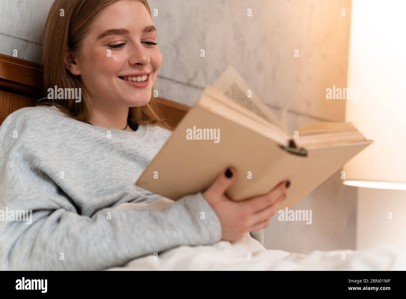 Photo of a positive happy beautiful young woman indoors at home in bed ...