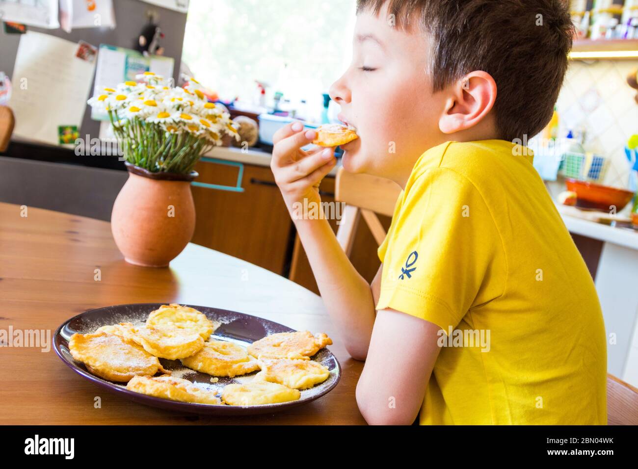 Boy child kid eating homemade fried battered apple fritters at home ...