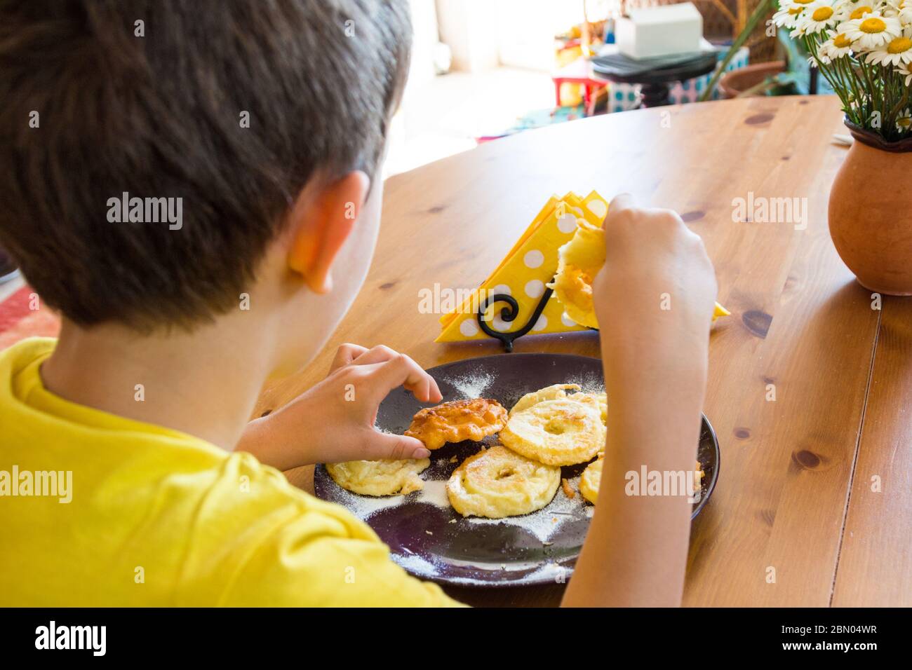 Boy child kid eating homemade fried battered apple fritters at home ...
