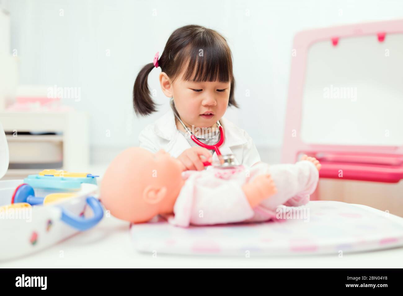 toddler girl pretend play doctor role at home against white background ...